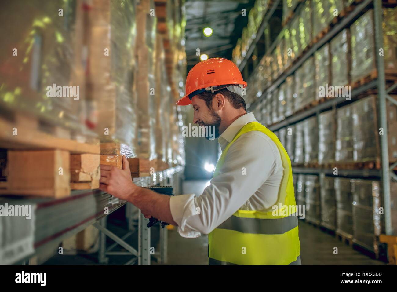 Warehouse worker in yellow vest fixing boxes on the shelves Stock Photo ...