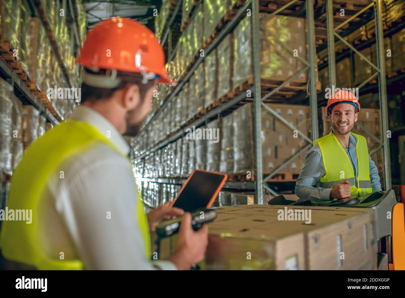 Two warehouse workers in helmets talking while working Stock Photo - Alamy