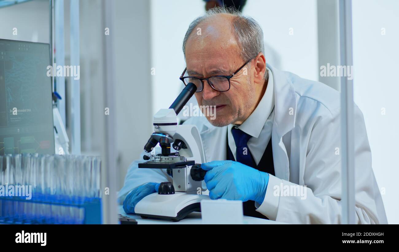 Laboratory scientist conducting experiment looking at microscope in ...
