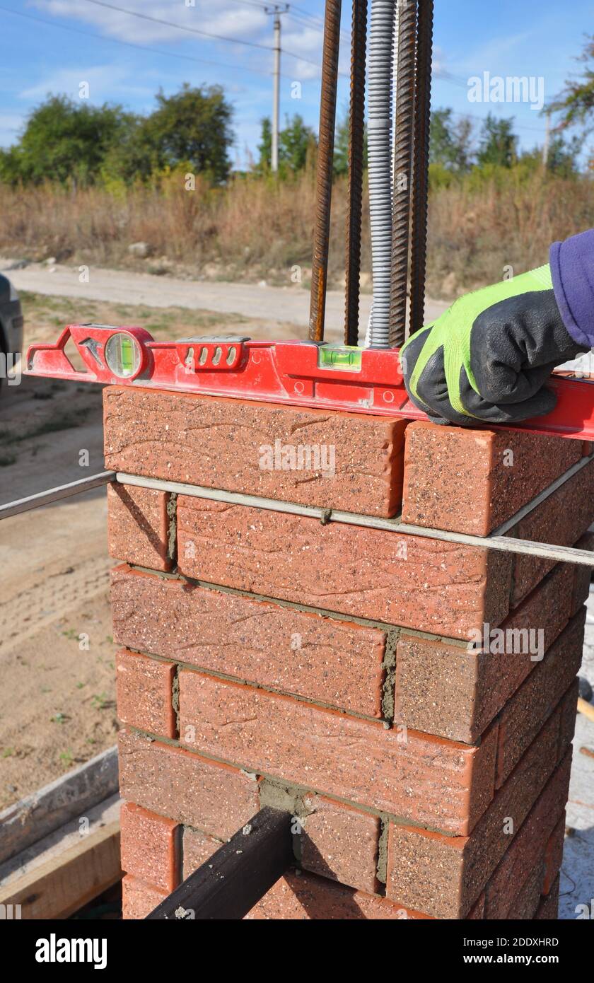 Builder laying brick on brick column and measuring with spirit level ...