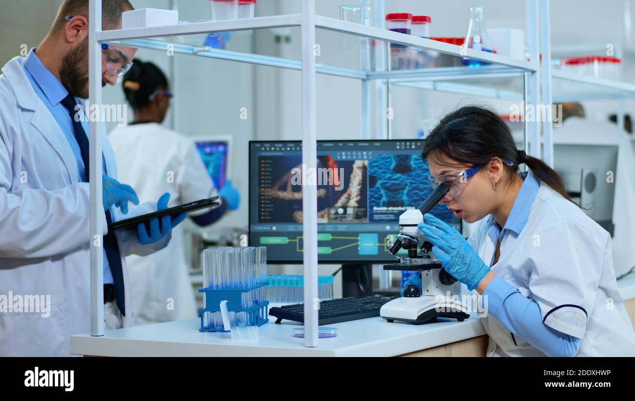 Scientist team checking virus development using microscope and writing ...