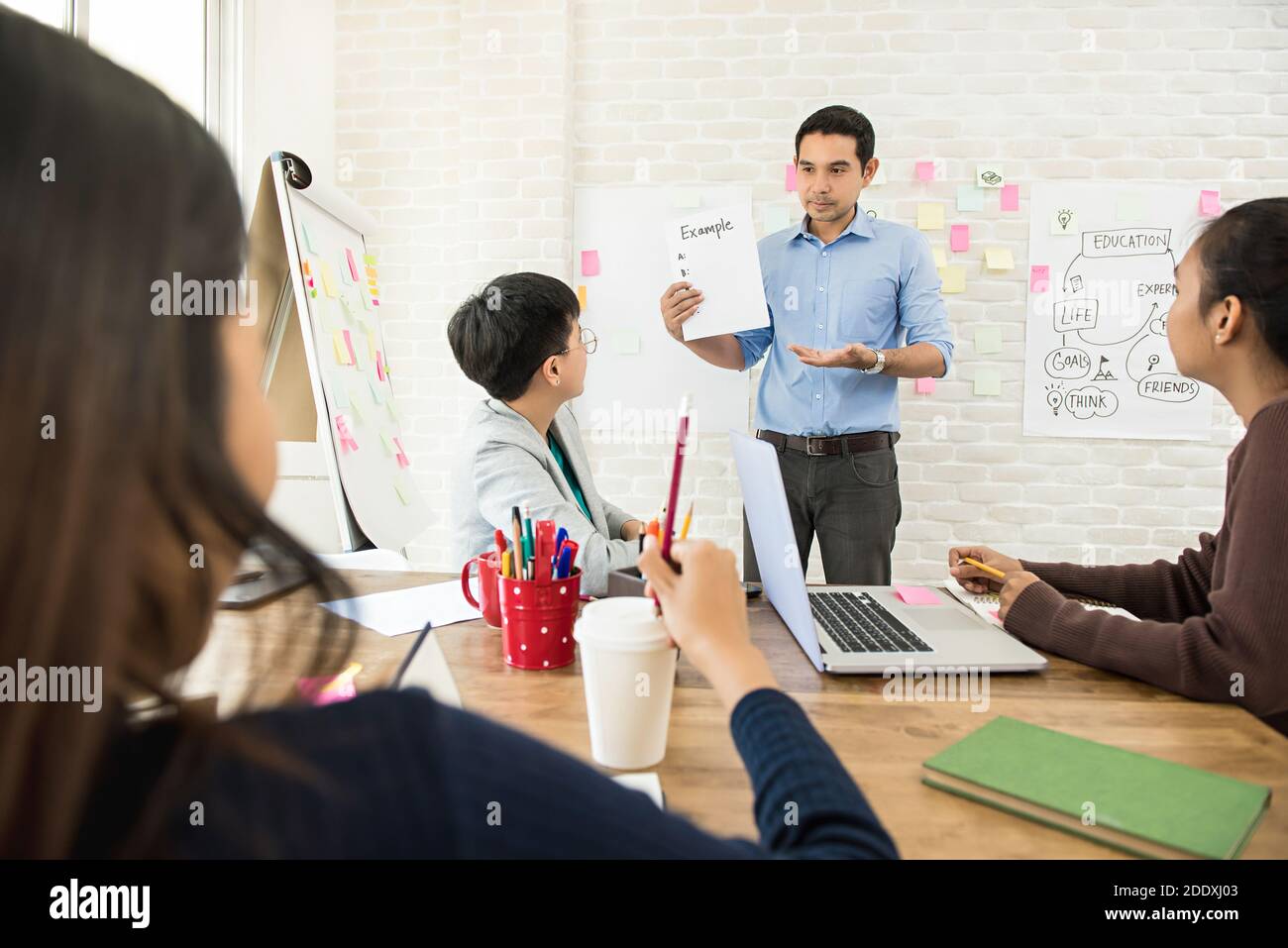 Asian male teacher showing and explaining example on paper to group of ...