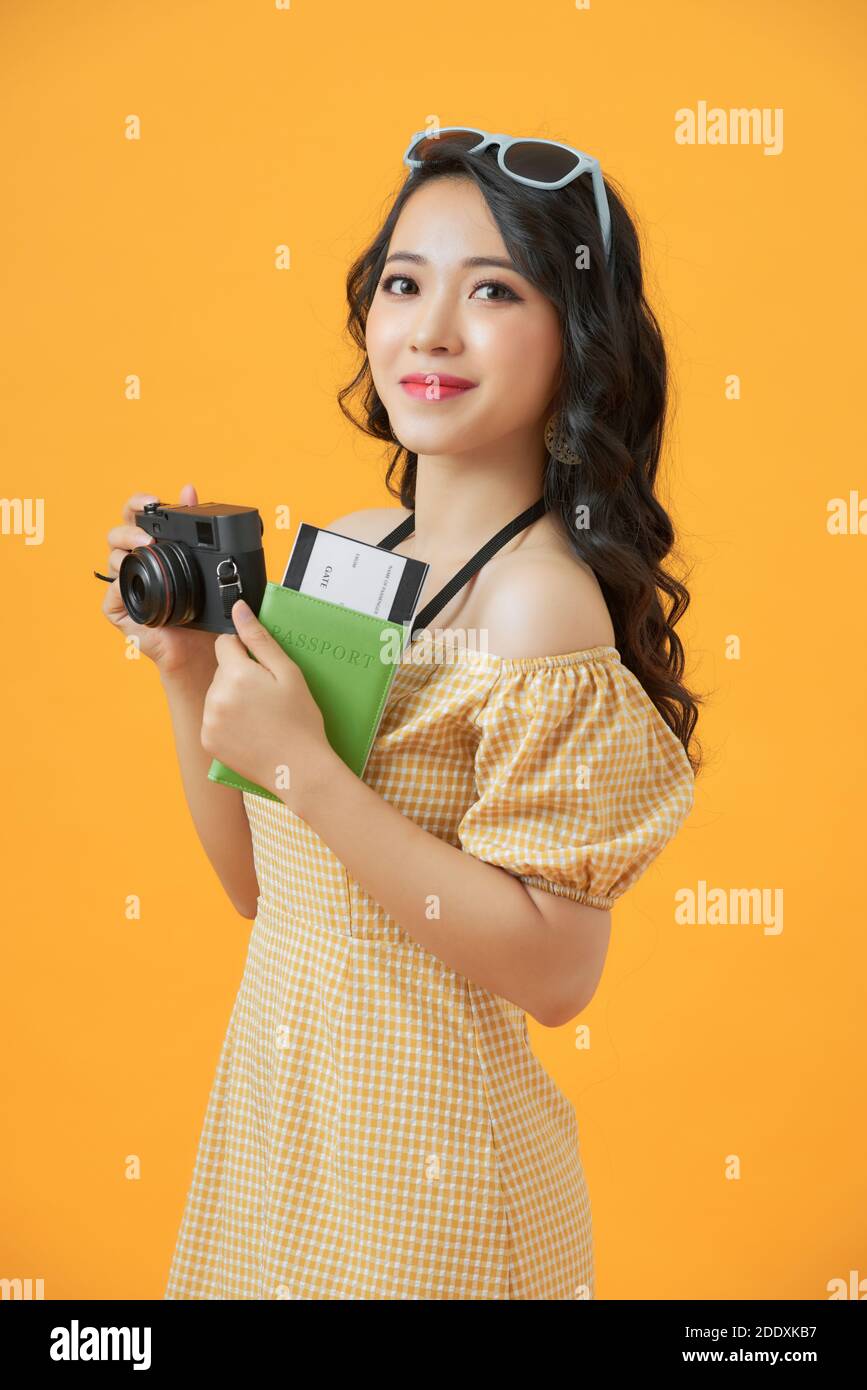 Image of happy asian young woman tourist standing isolated over yellow background holding camera ...