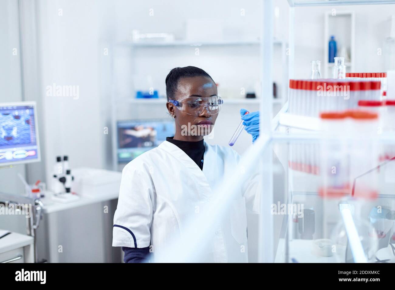 African scientist in protective glasses looking at test tube with ...