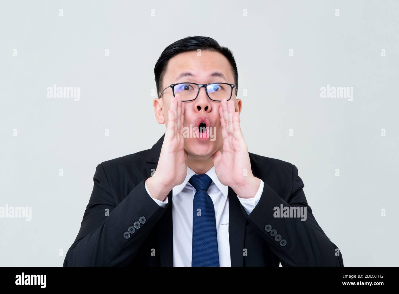 Excited young Asian businessman shouting with hands cupped around mouth ...