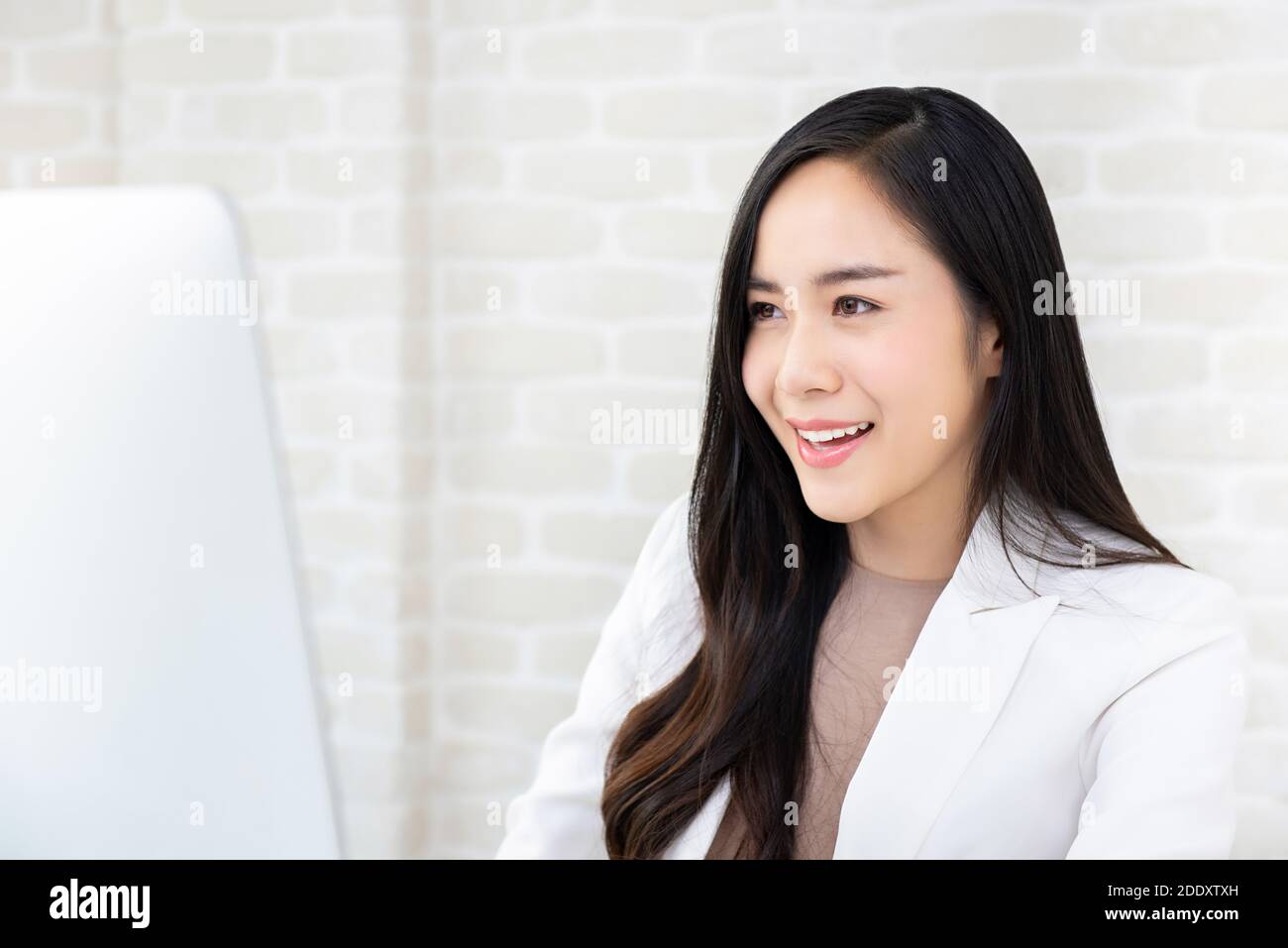 Beautiful smiling young Asian woman in white suit working on computer at the office Stock Photo ...