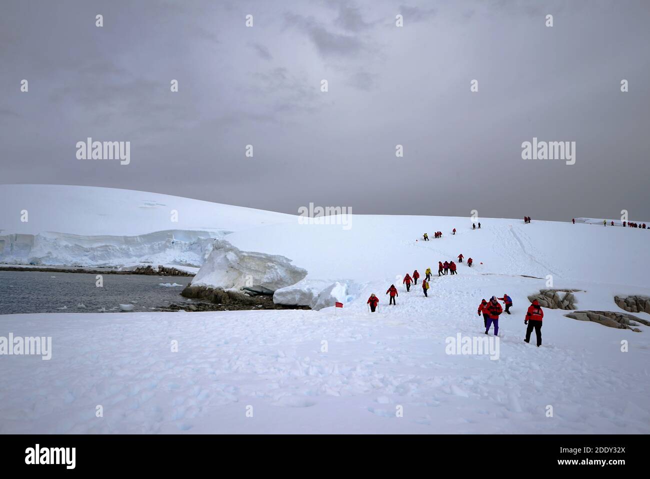 There is the sea next to the thick ice sheet. Tourists are walking on ...