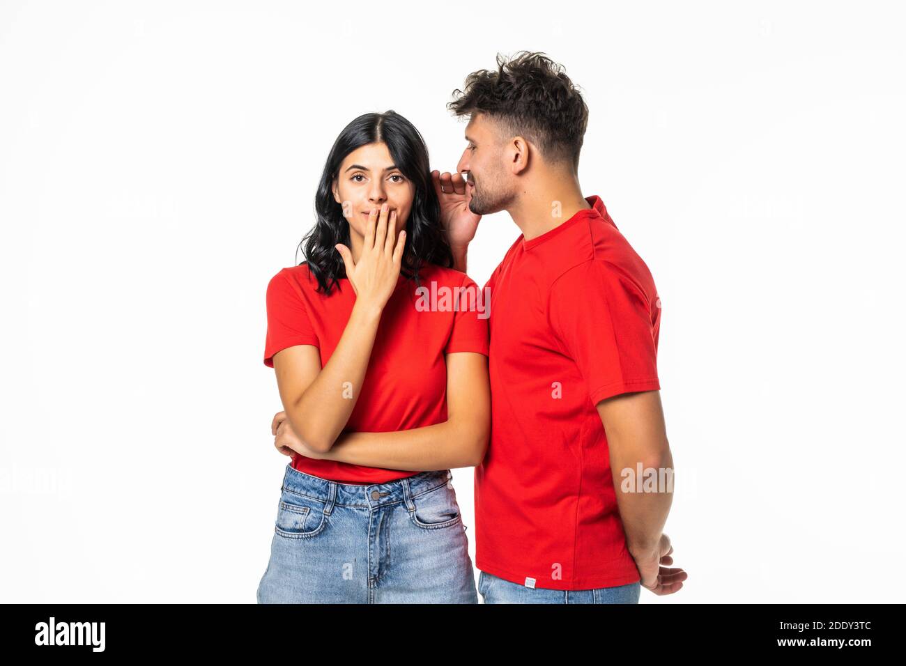 Portrait of an astonished young couple telling secrets standing ...