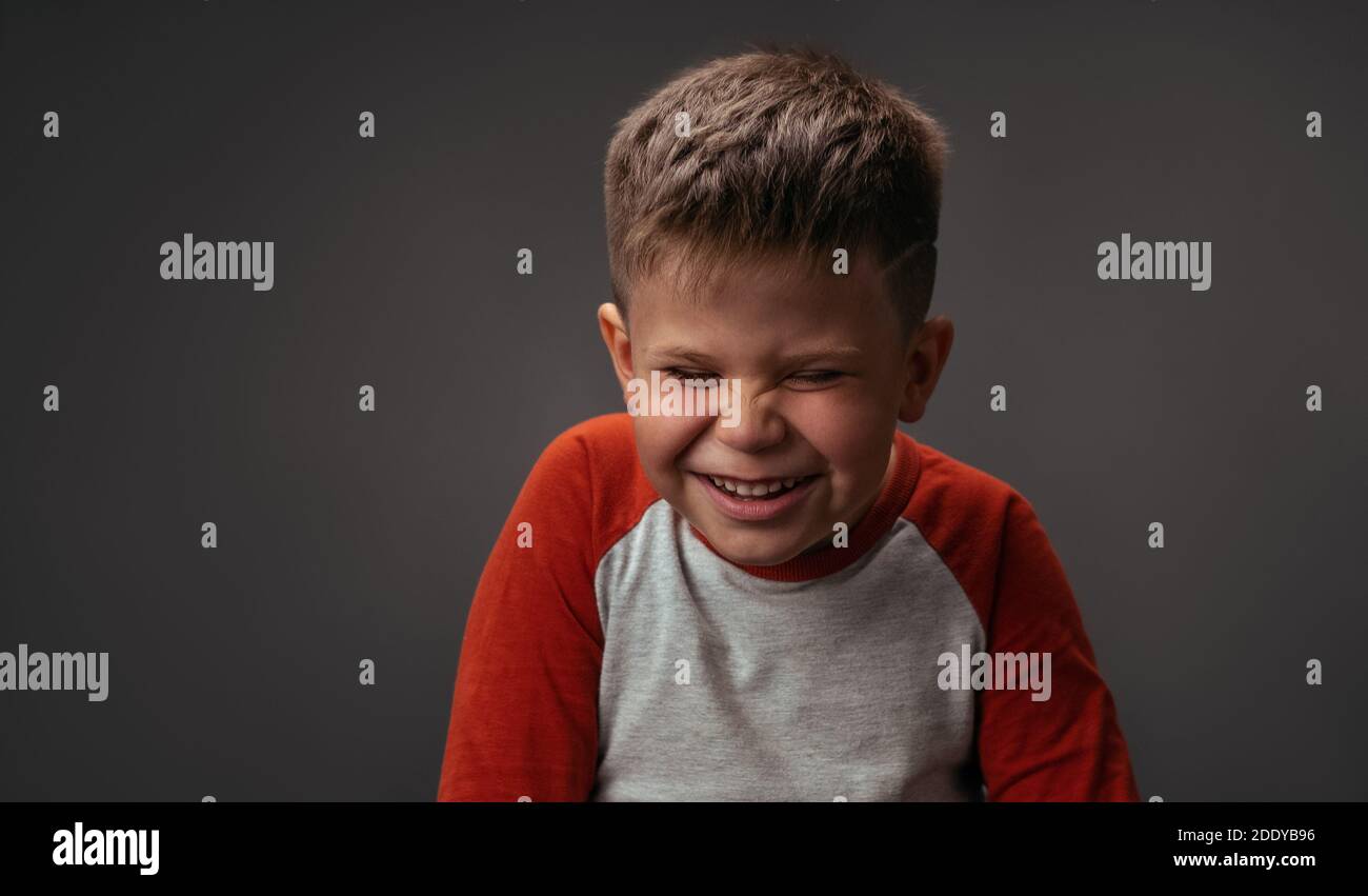 Giggling laughing little boy in red shirt with eyes shut. Happy kid on ...