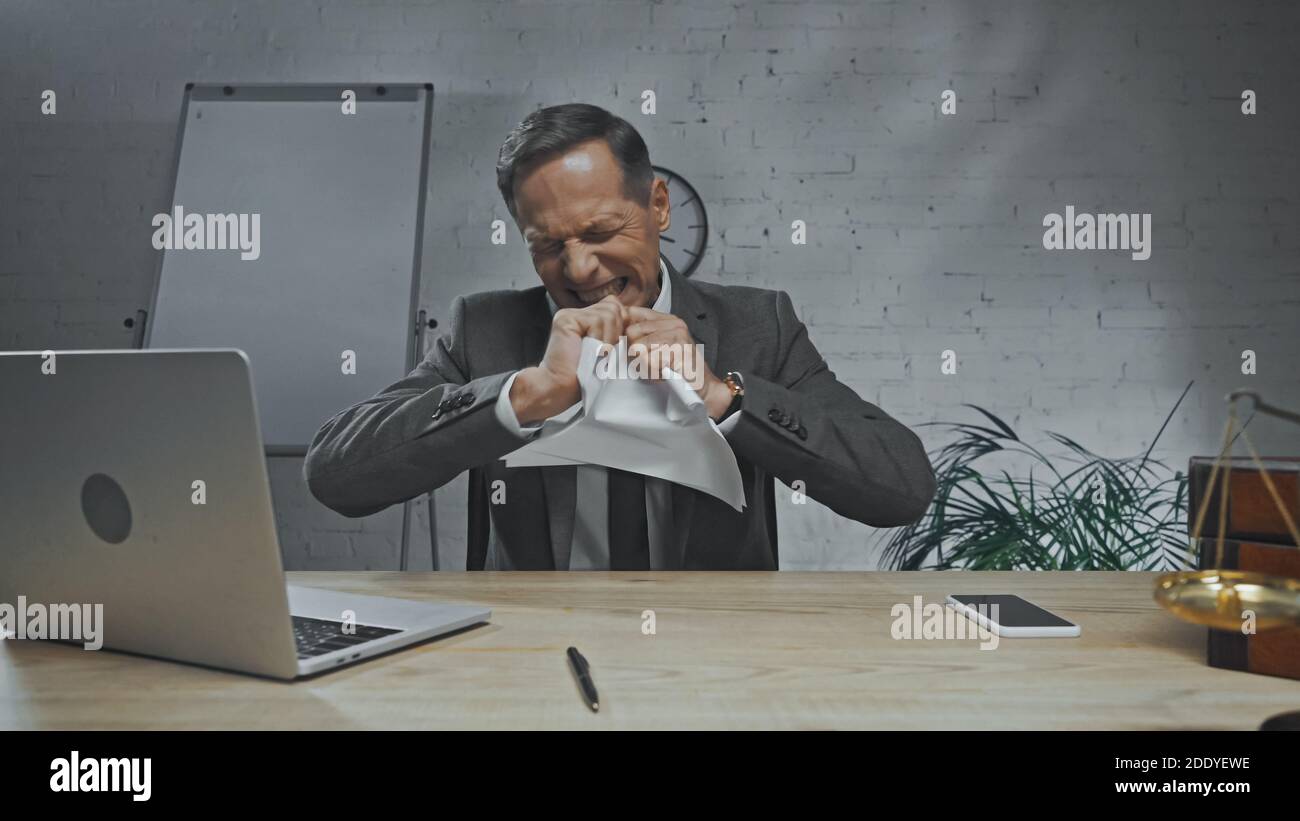 Angry insurance agent tearing papers near devices and scales on blurred ...