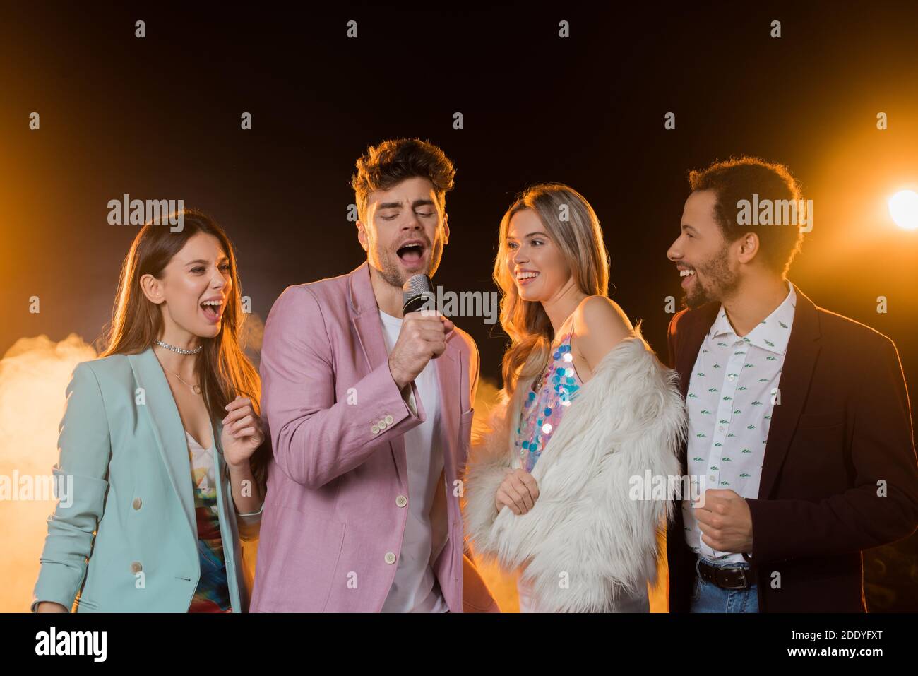 man singing while in microphone near multicultural friends on black ...