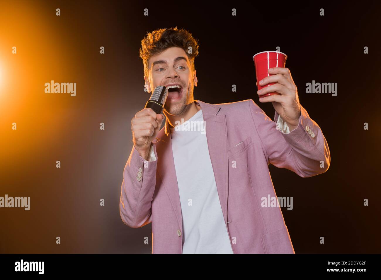 man singing while holding microphone and plastic cup on black Stock ...