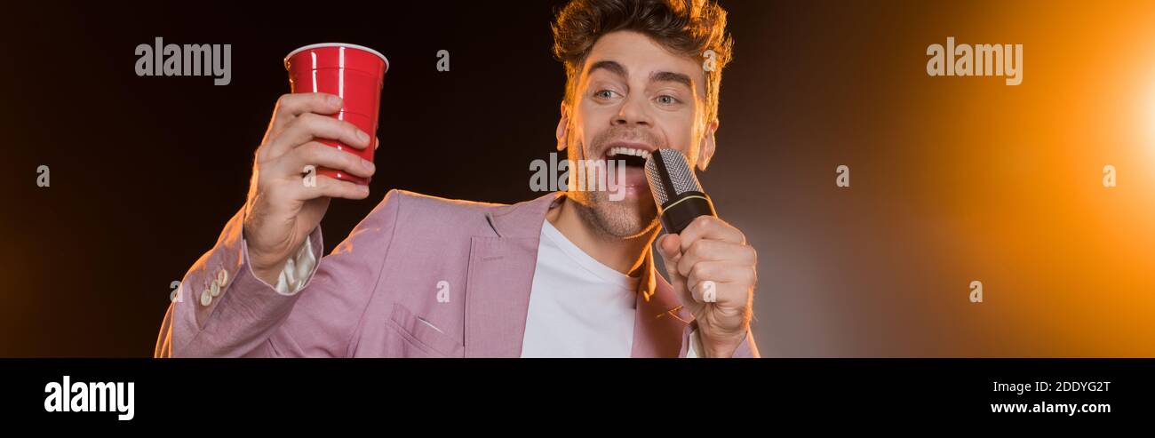 man singing while holding microphone and plastic cup on black, banner ...