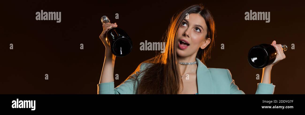 surprised brunette woman in jacket holding bottles with champagne on ...