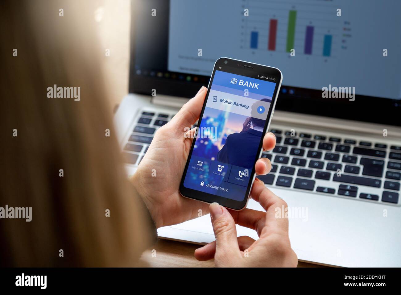 Mobile banking app on phone screen. Young woman in front of laptop ...