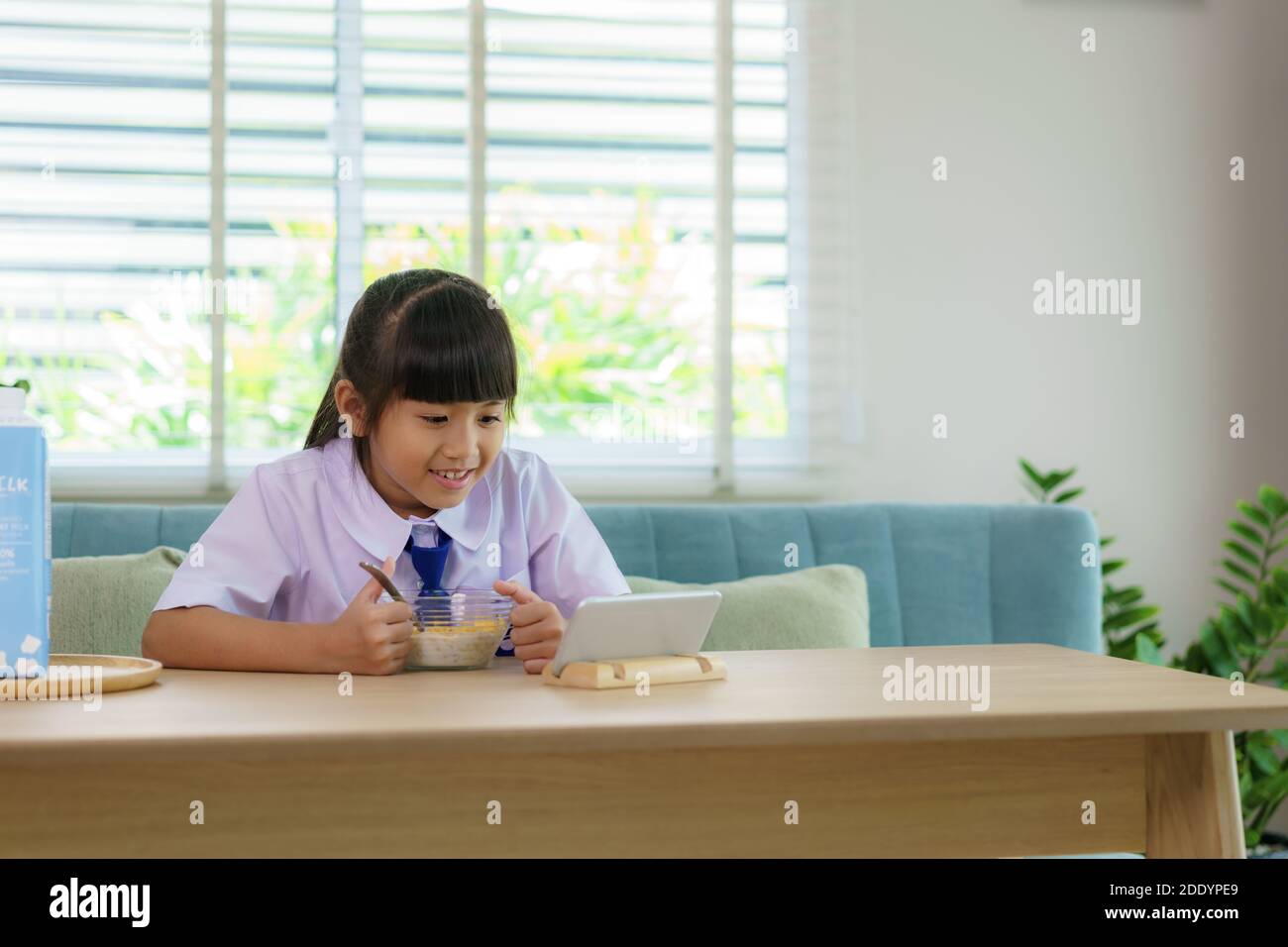 Asian elementary school student girl in uniform eating breakfast ...