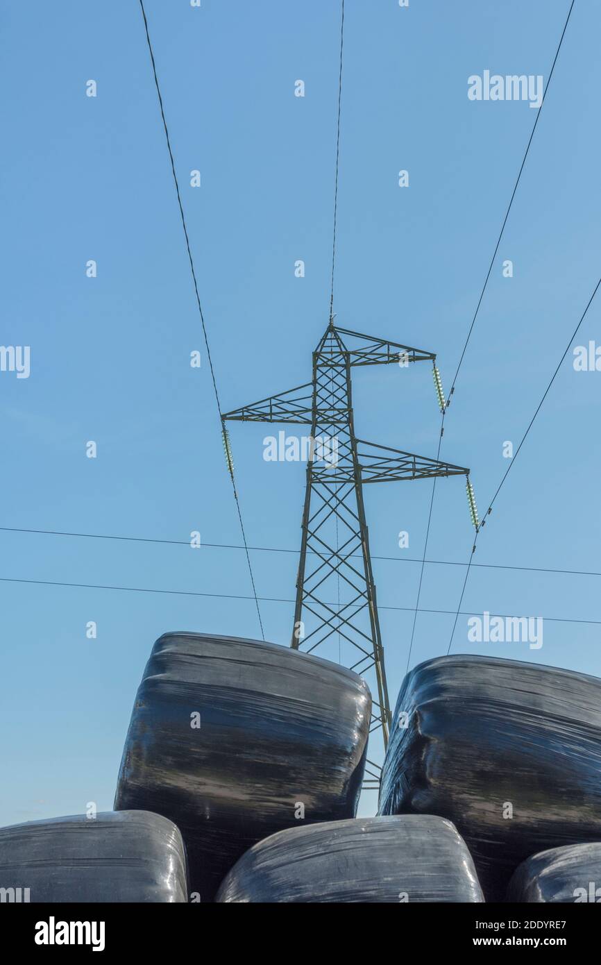 High voltage electricity pylon with polywrap hay bales against blue ...