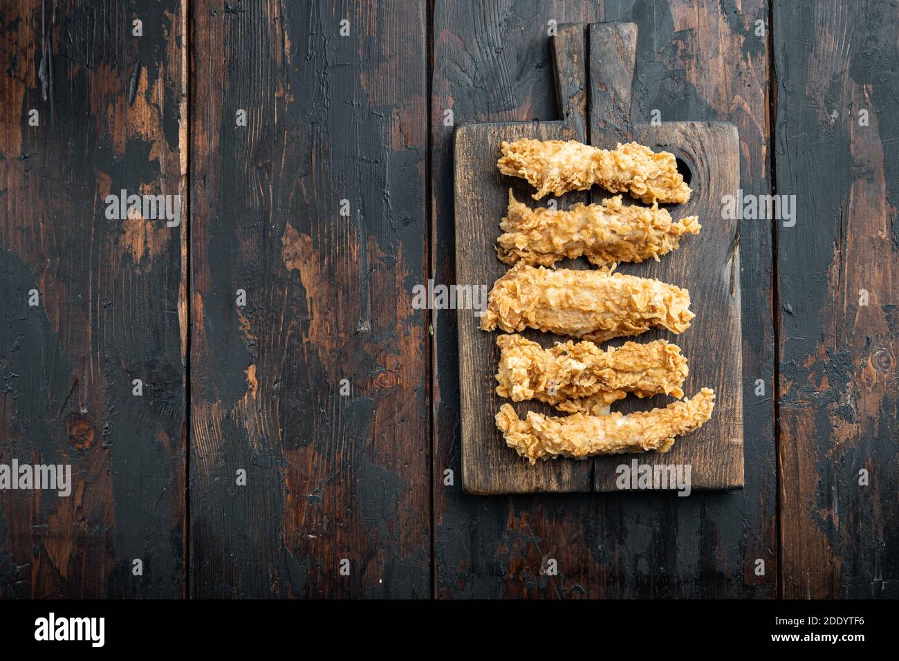 Chicken breaded fillet stripes on old dark wooden table, top view, with ...