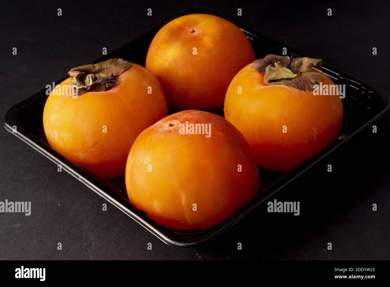ripe persimmons in a black box on black background Stock Photo - Alamy