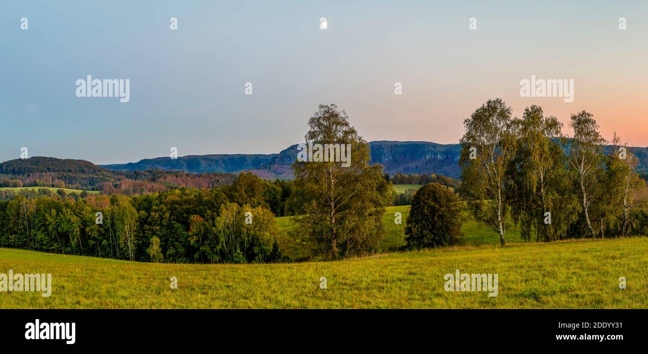 Green, tree-lined fields in front of mountains on the horizon with an ...