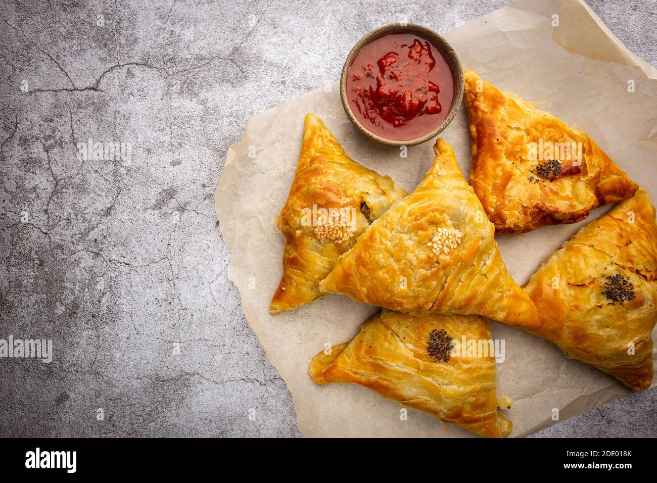 Samsa or samosas with meat and vegetables with tomato sauce on gray background. Traditional ...