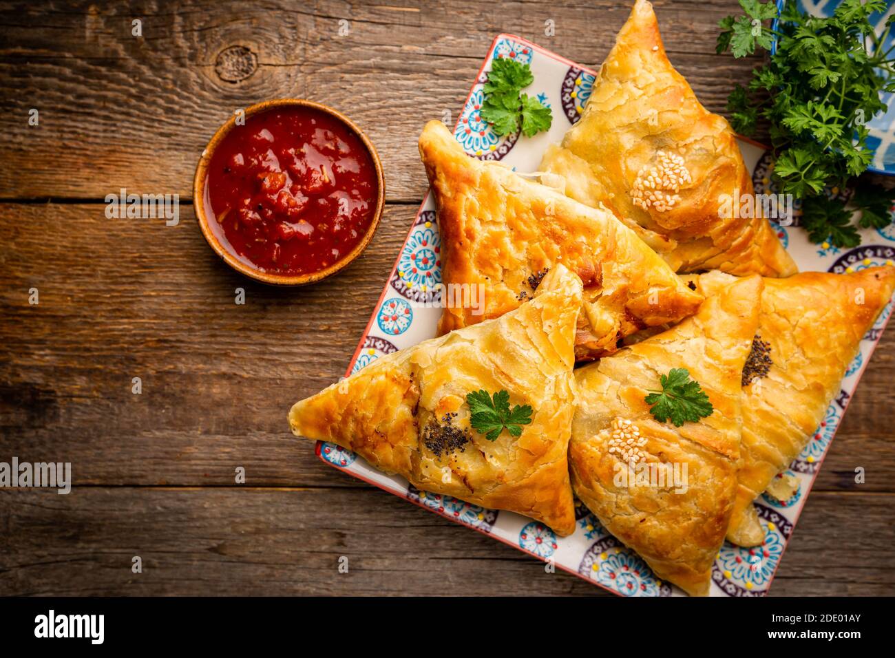 Samsa or samosas with meat and vegetables with tomato sauce on wooden background. Traditional ...
