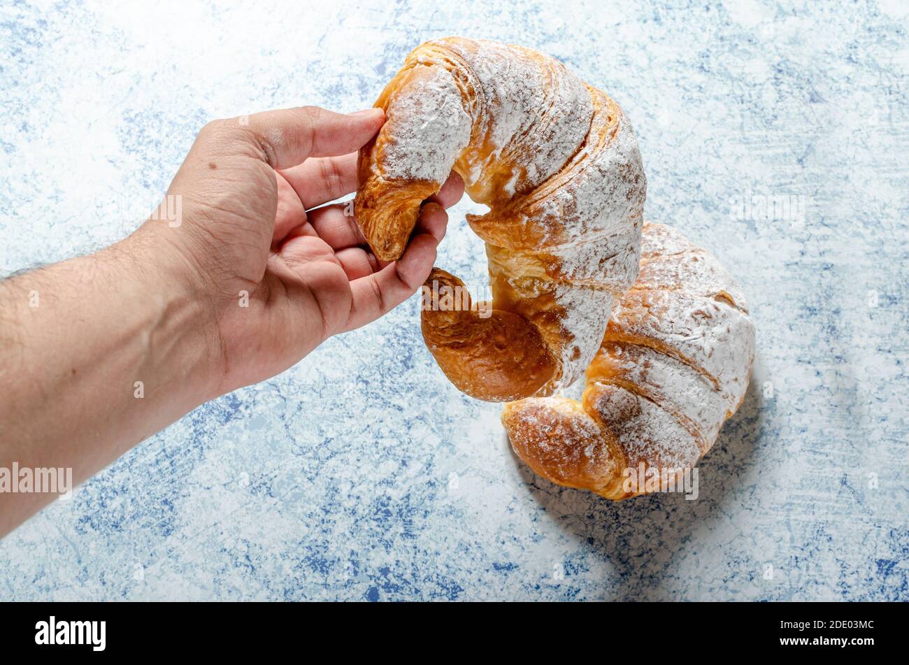 Hand holding a freshly baked croissant with icing sugar on a textured ...