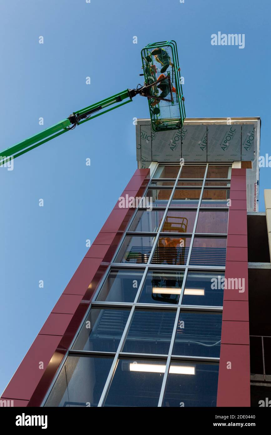 Workers in a cherry picker boom lift reach the top of a building in ...