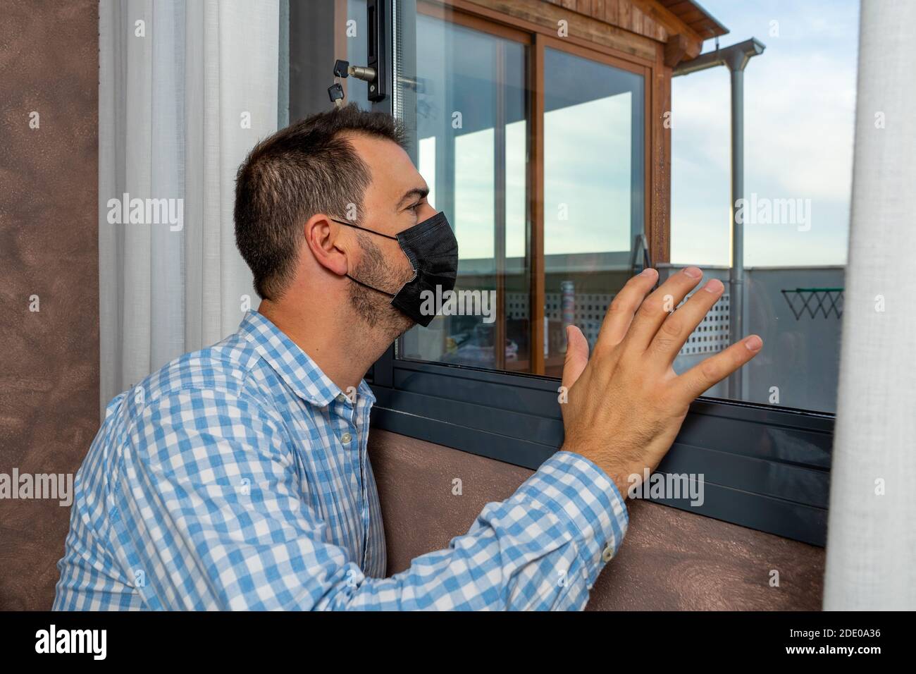 Sick man from coronavirus looking out the window and wearing mask for protection and recovery ...