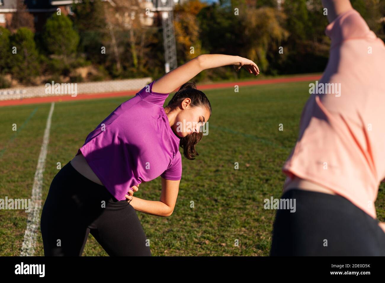 two young women doing stretching on the grass of a running track before ...