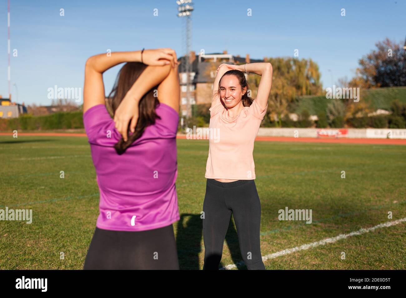 two young women doing stretching on the grass of a running track before ...