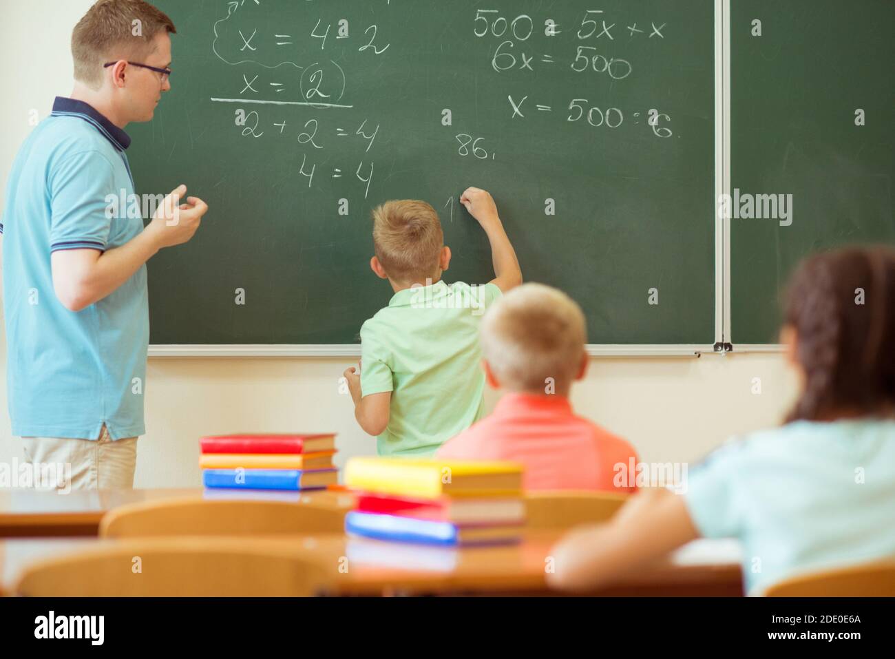 School boy with his teacher at the blackboard solving at math lesson in ...