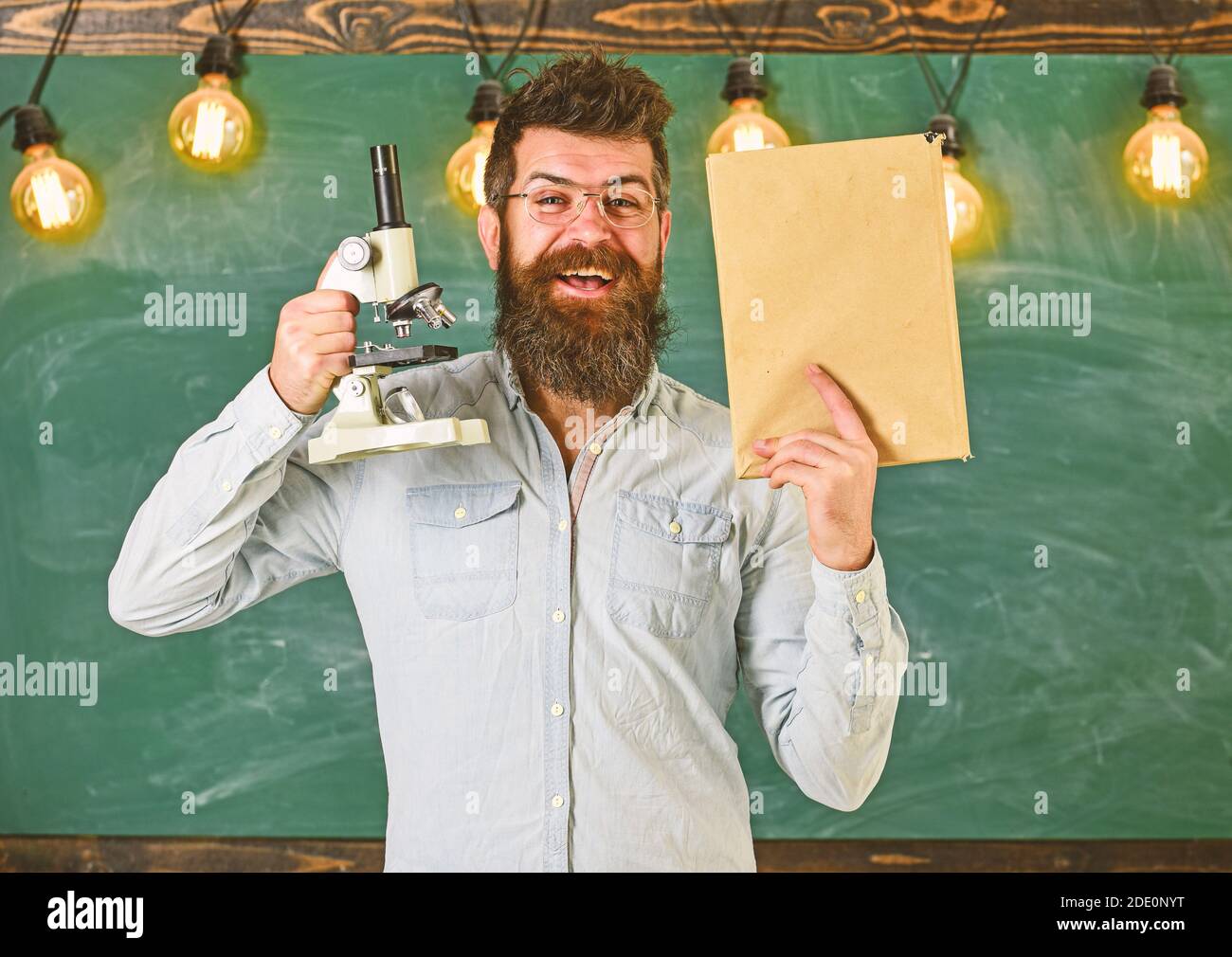 Teacher of biology in eyeglasses holds book and microscope. Biology ...