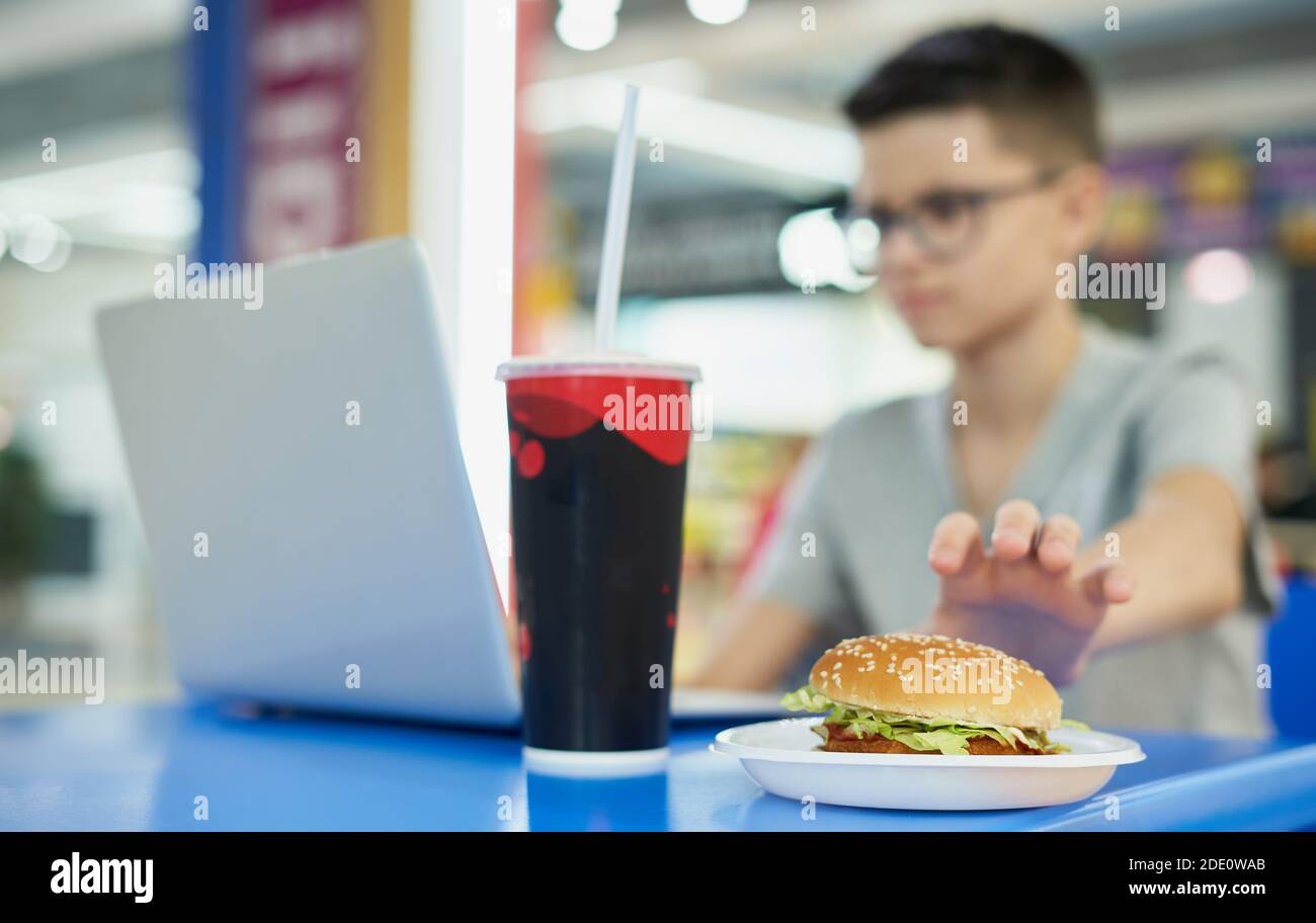 Teenage boy takes a burger while having lunch in a restaurant. Child ...