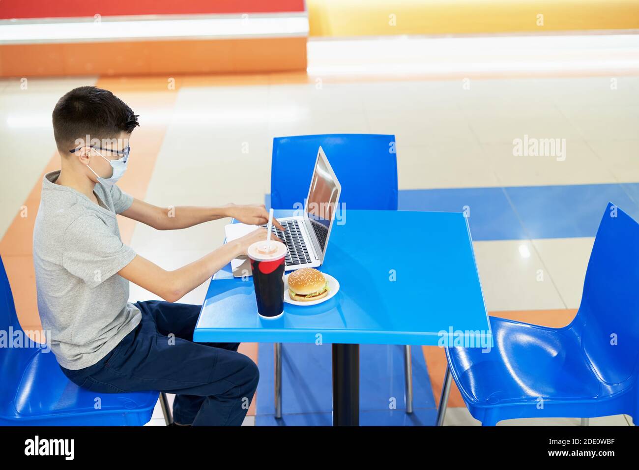 Teenager in fast food restaurant wearing protective mask with laptop ...