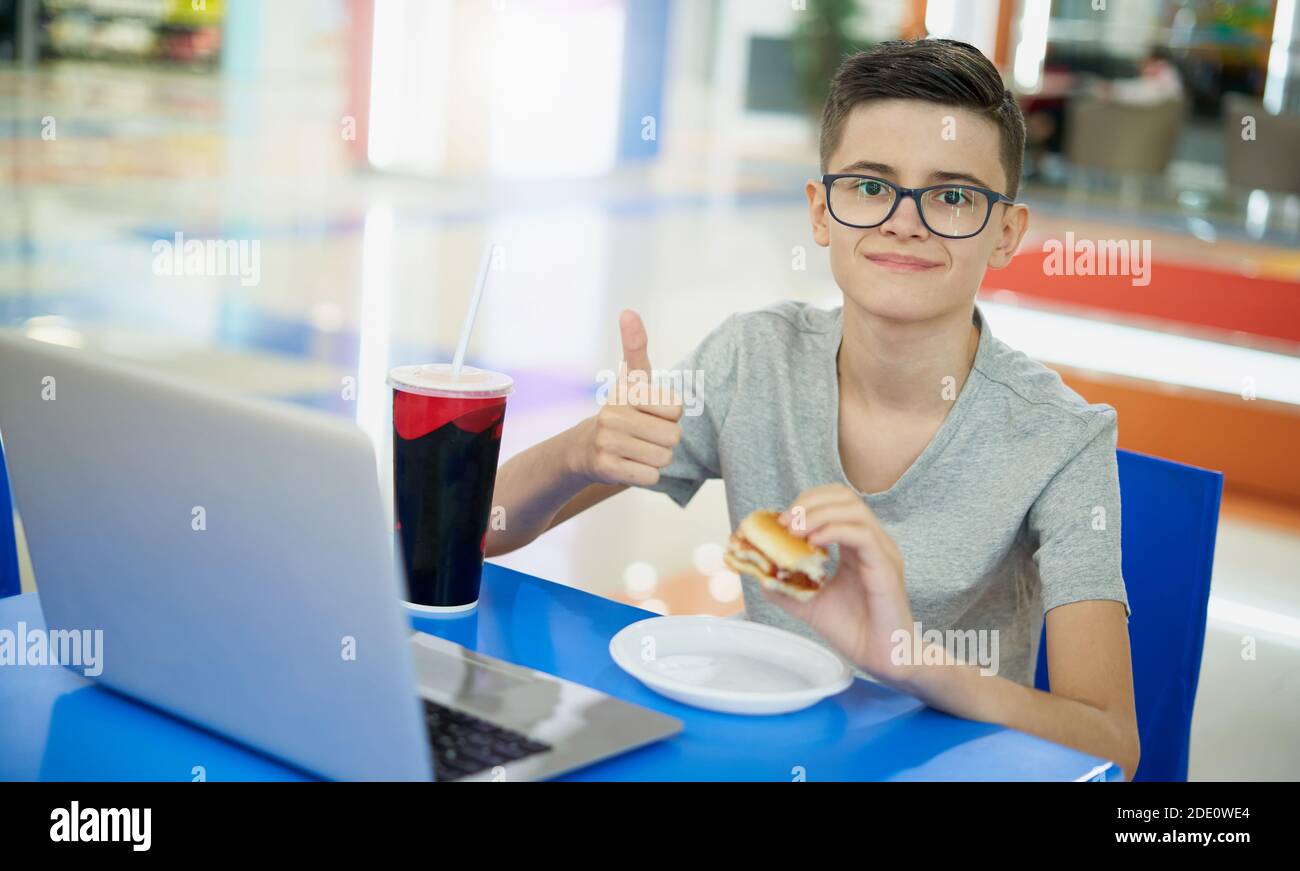 Portrait of a teenage boy eating a burger and showing thumbs up from ...