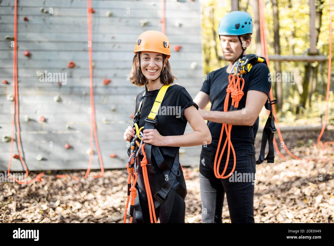 Male instructor puts protective climbing equipment on a young woman at ...