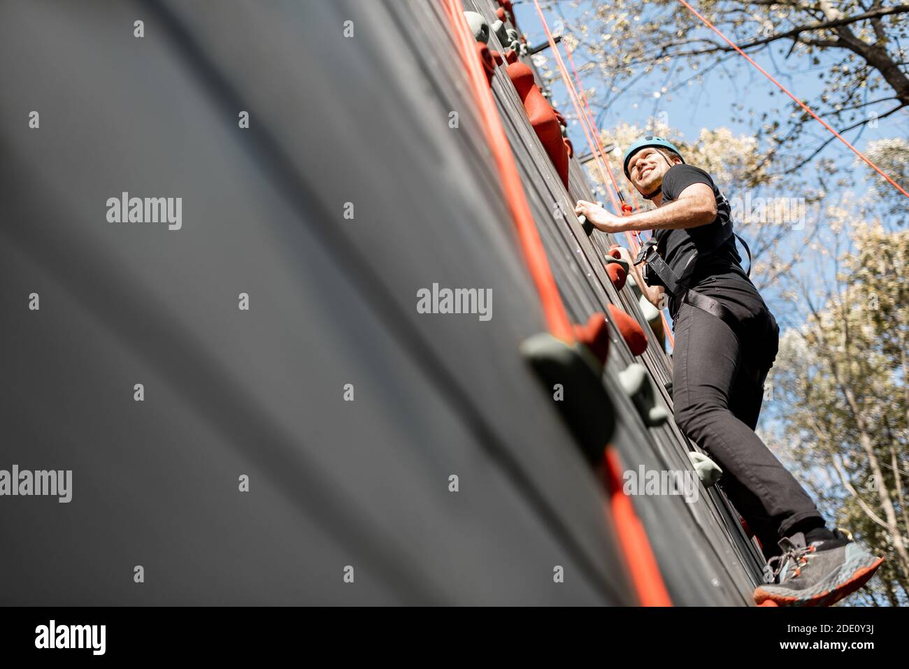 Well-equipped man climbing the wall outdoors in the park for sports ...