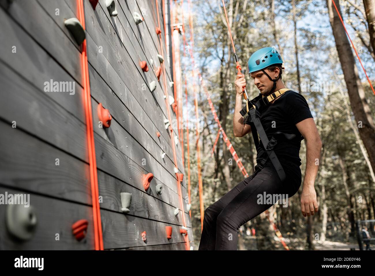 Well-equipped man climbing the wall outdoors in the park for sports ...