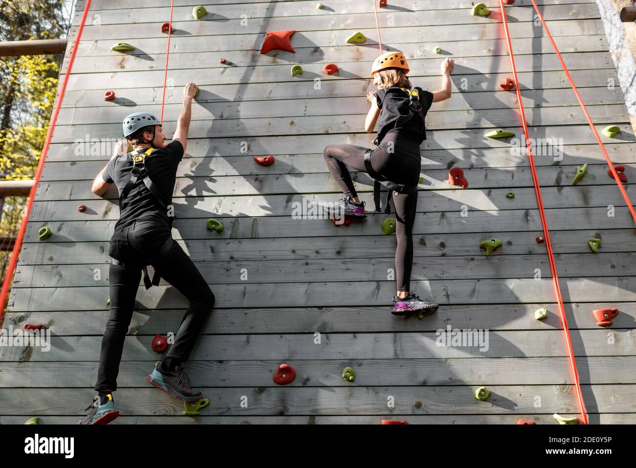 Well-equipped man and woman climbing the wall outdoors in the park for ...