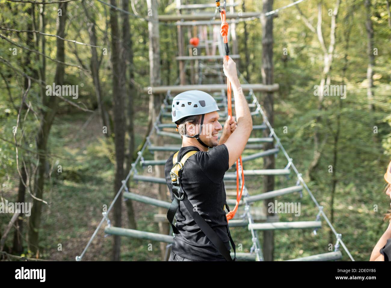 Well-equipped man having an active recreation, climbing in a rope park ...