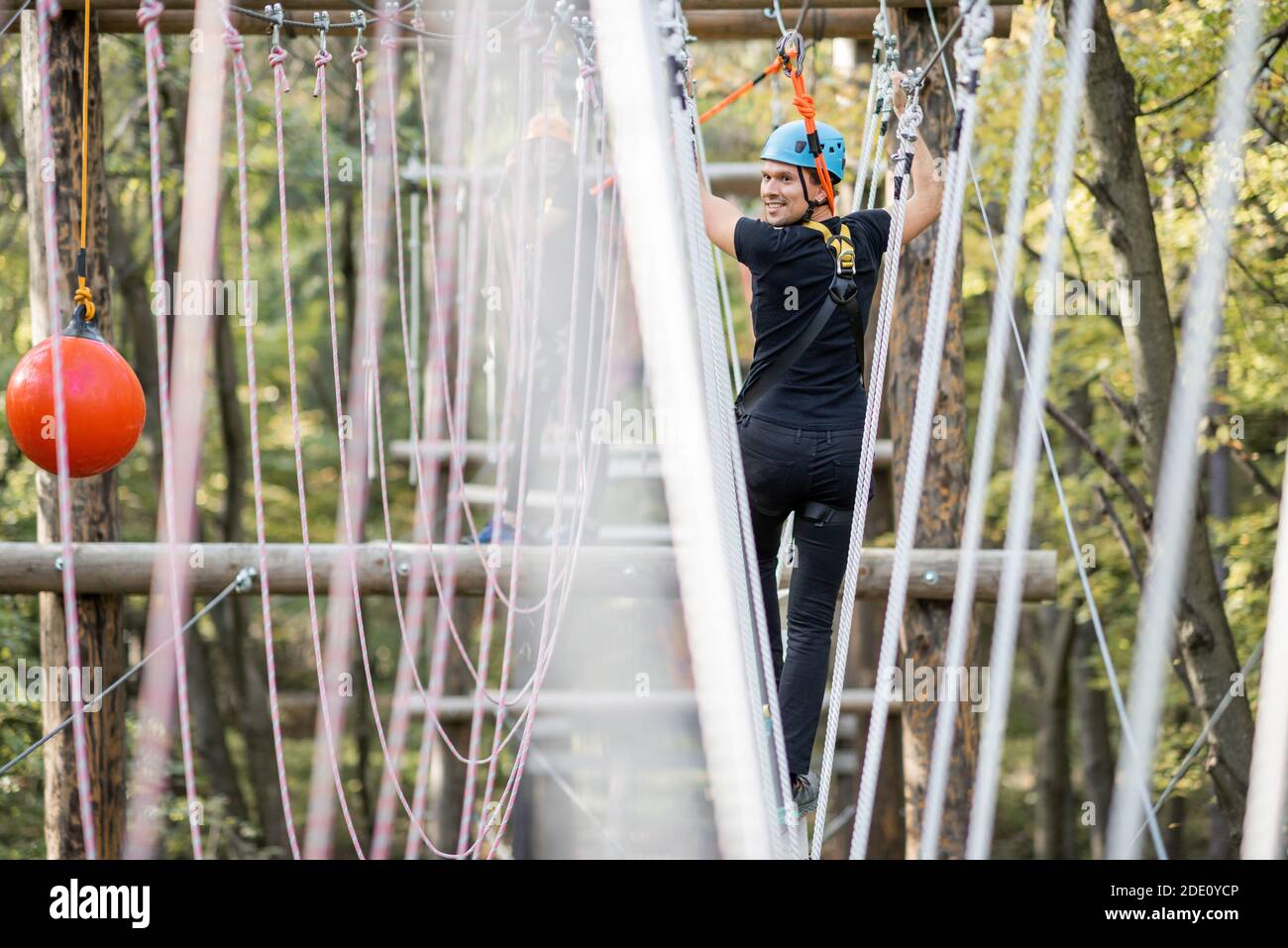 Well-equipped man having an active recreation, climbing in a rope park ...