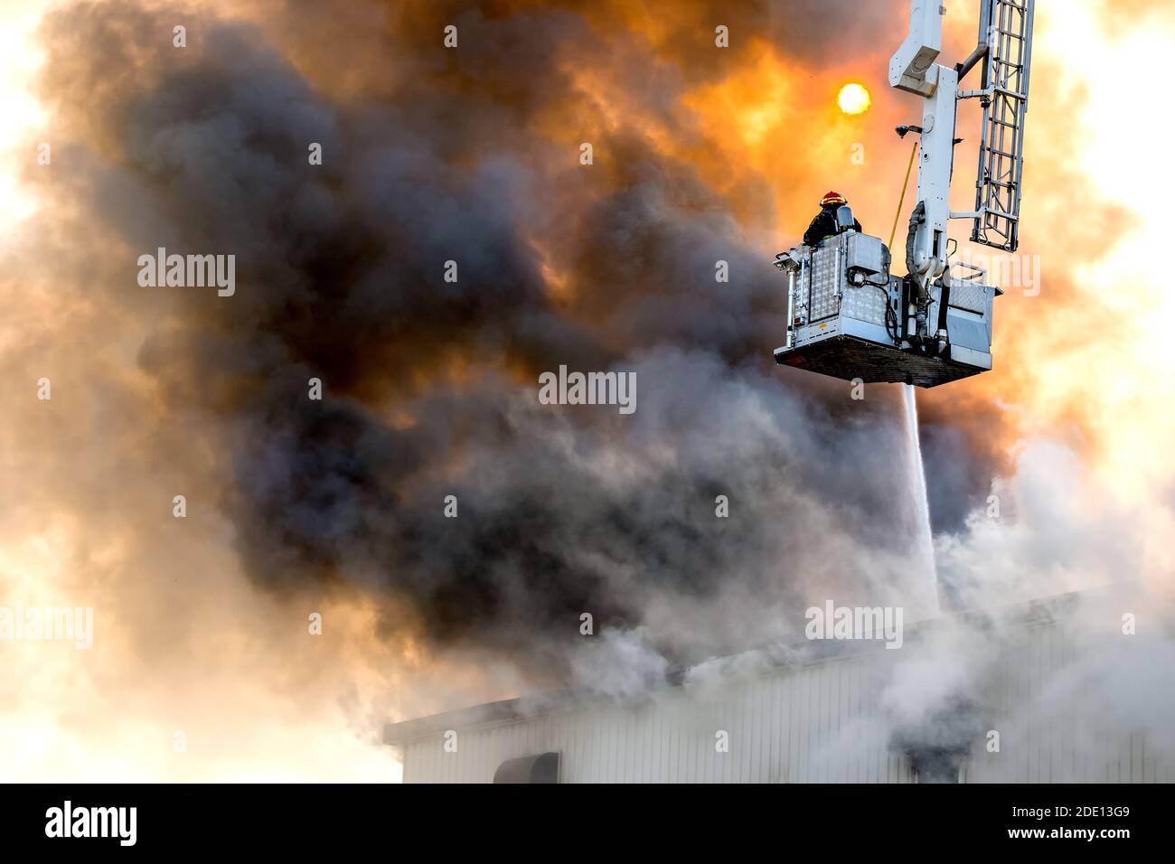 Fireman fighting a building fire from bucket above building. A hose ...