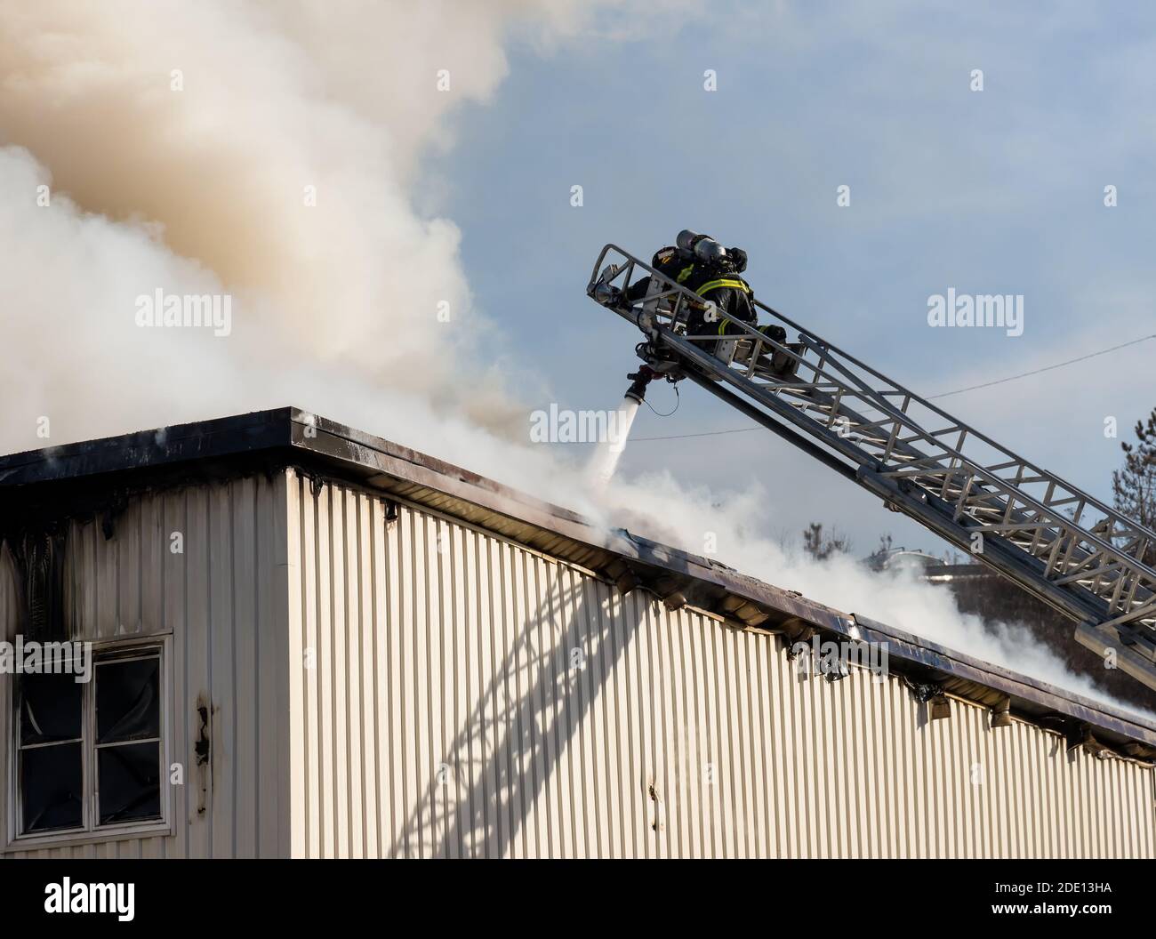Fireman fighting a building fire at the top of an extended ladder. A ...