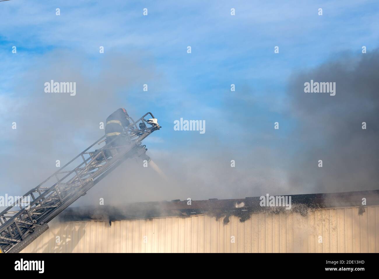 Fireman fighting a building fire at the top of an extended ladder ...