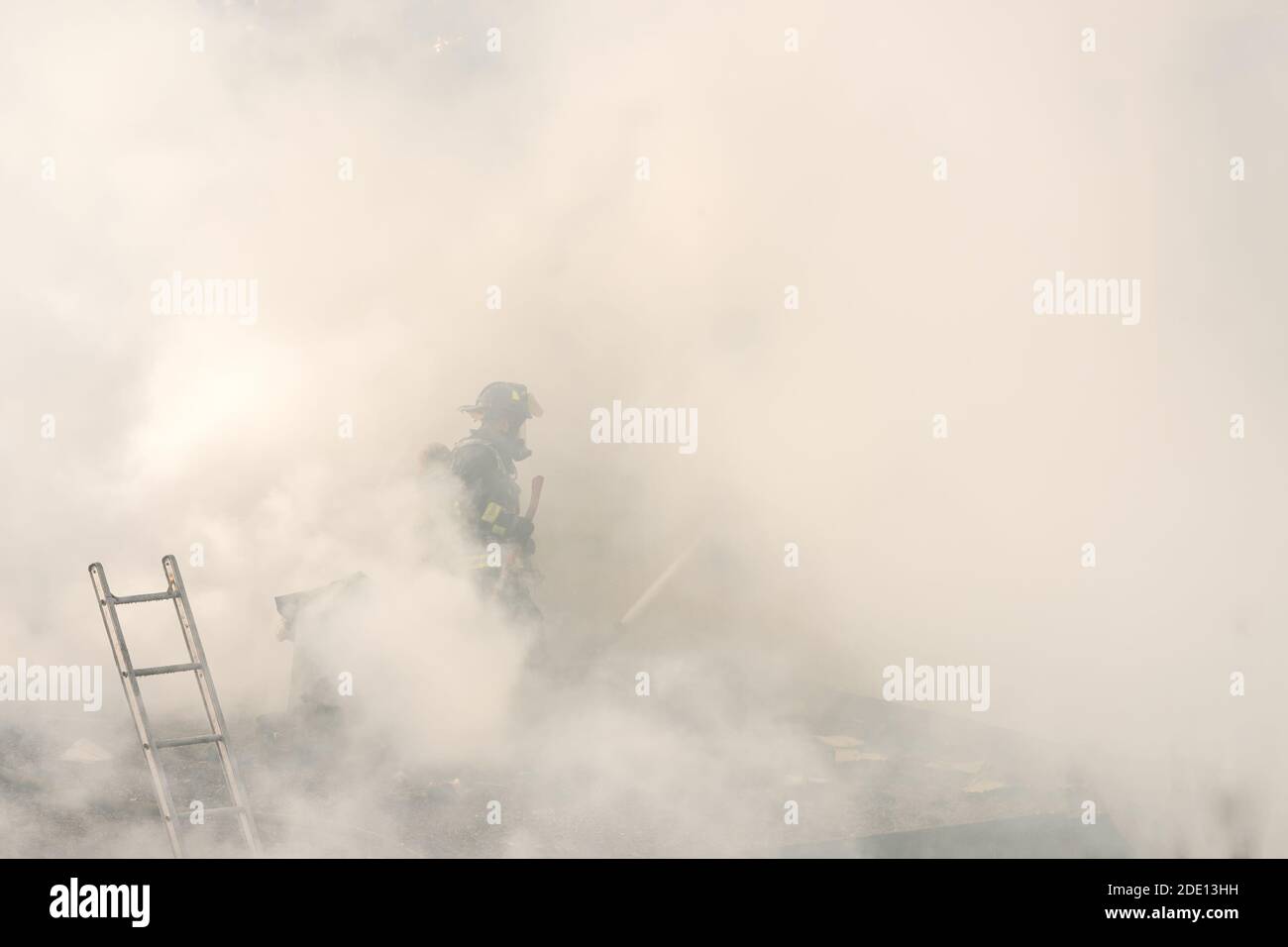 A fireman on the roof of a burning building. He is barely visible ...