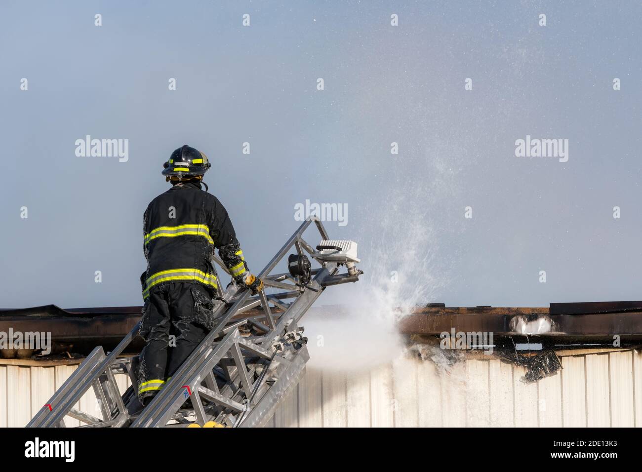 Fireman fighting a building fire at the top of an extended ladder. A ...