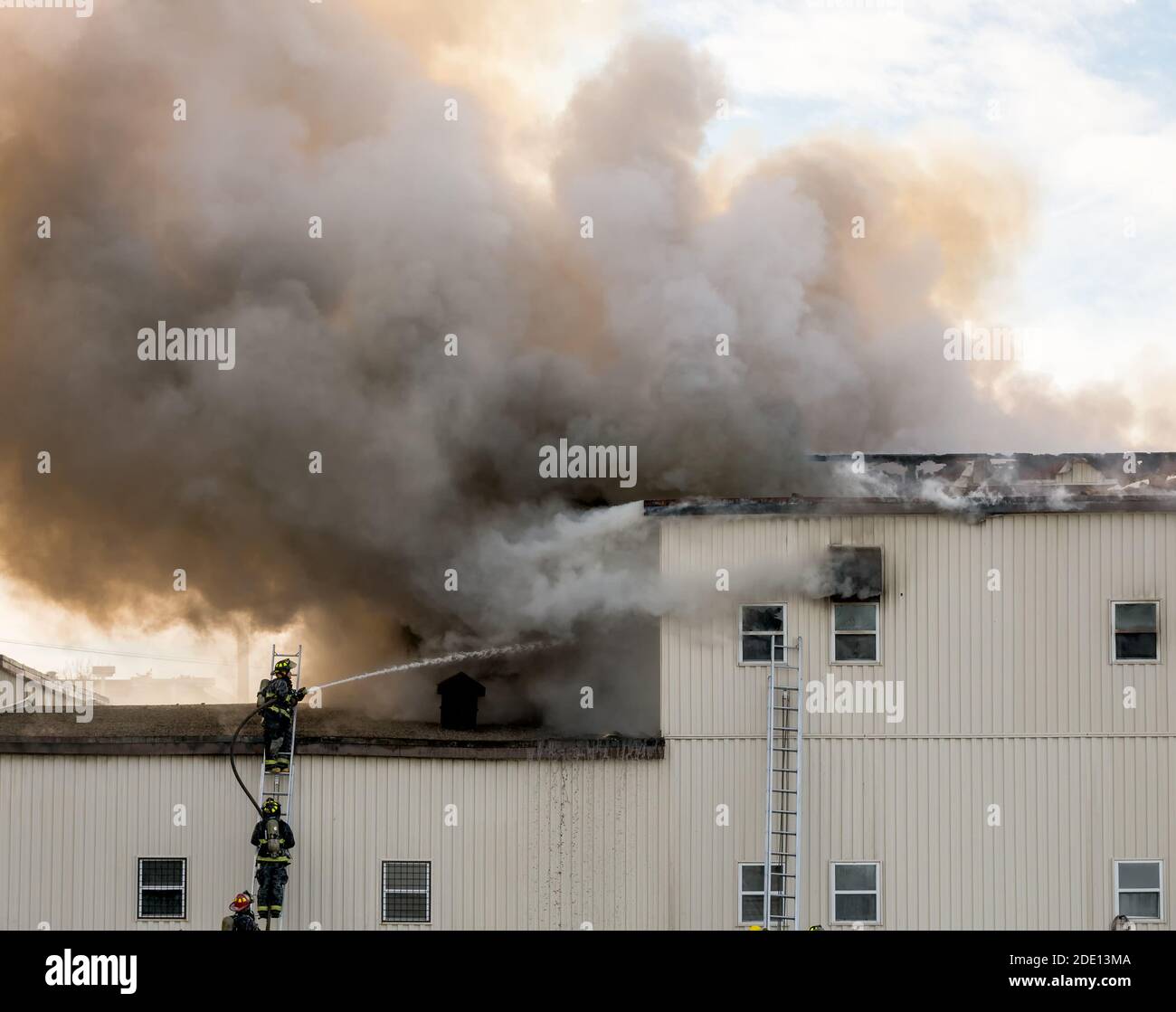 Firemen fighting a fire. One fireman at the top of a ladder with a hose ...