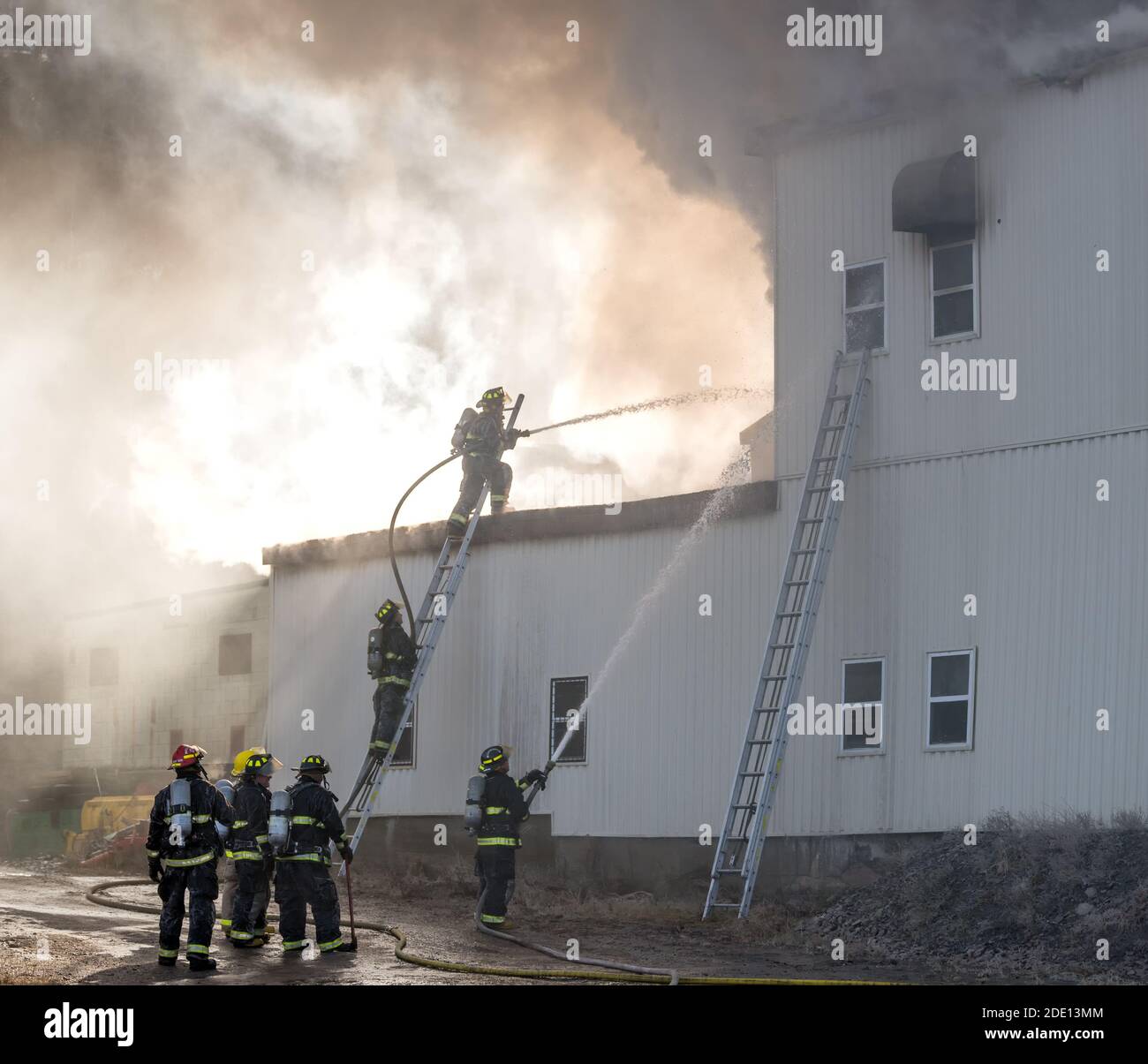 Firemen fighting a fire. One fireman at the top of a ladder with a hose ...