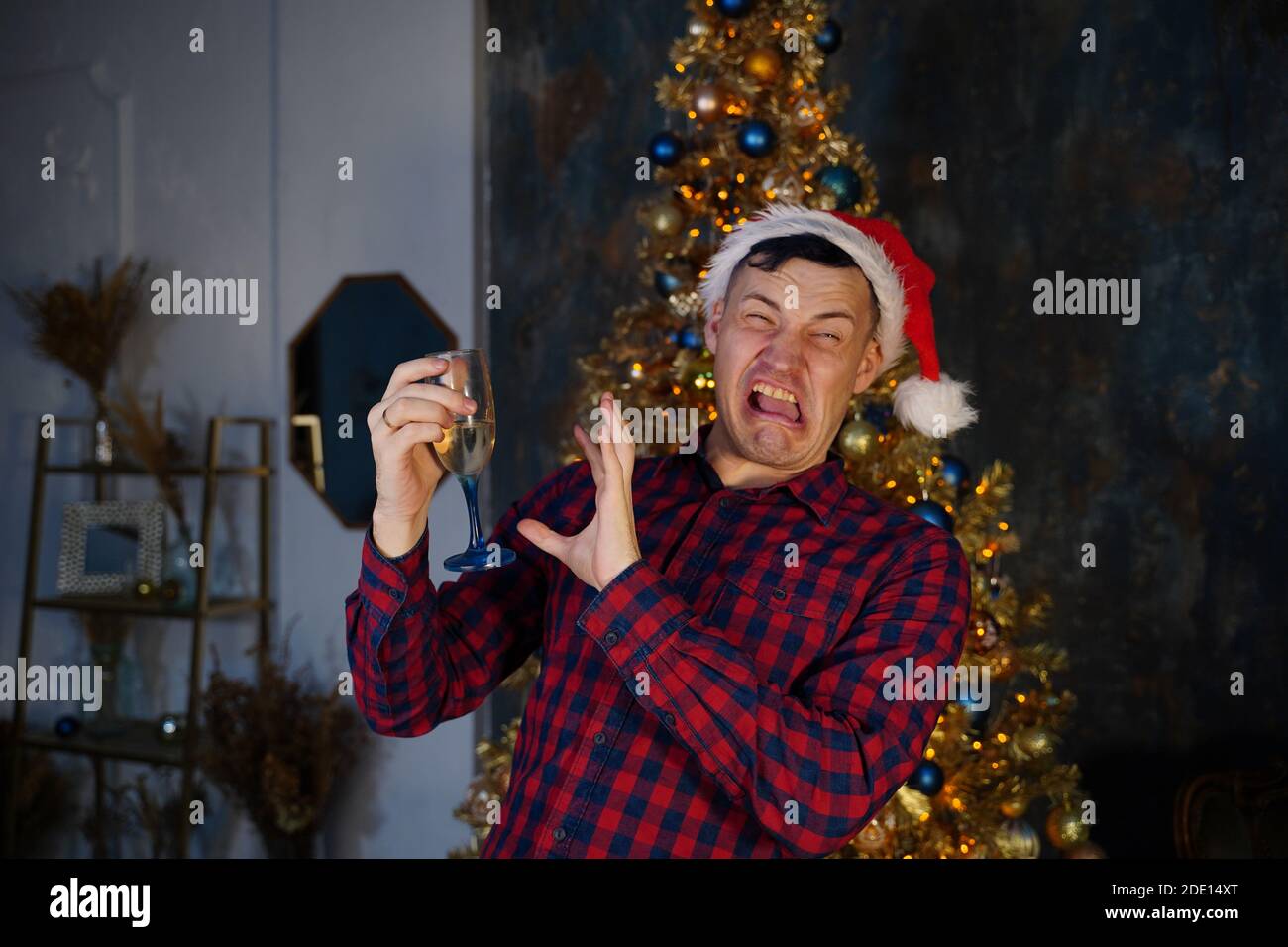 Young man in santa hat drinks champagne and grimaces from alcohol on ...